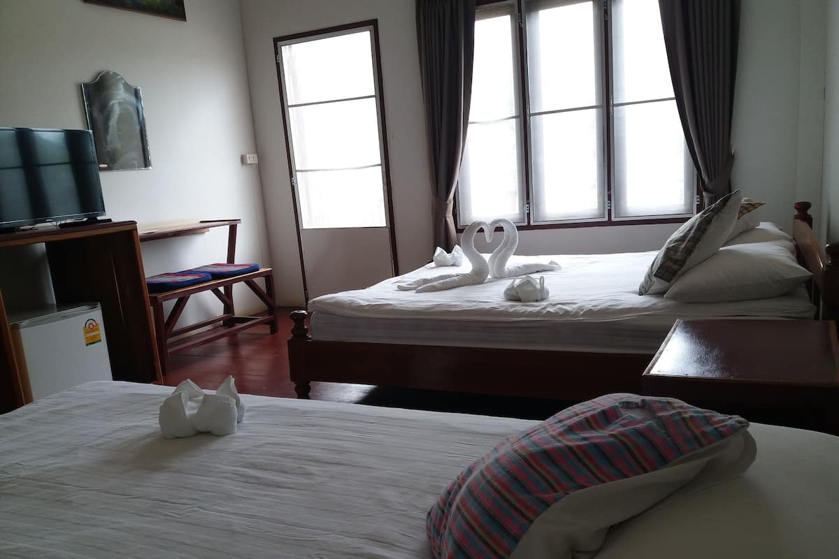 Quarto de hotel com duas camas, televisão, pequeno frigorífico e janela com cortinas.
