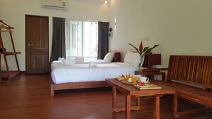 Quarto de hotel com uma cama grande, um banco de madeira, uma mesa pequena com café da manhã e uma janela com cortinas.