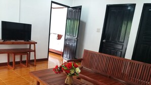Quarto com um banco de madeira, uma mesa pequena com um vaso de flores, uma televisão em um suporte e duas portas pretas.