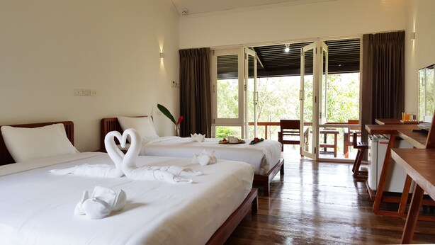 Quarto de hotel com duas camas, área de refeições e vista para o verde.