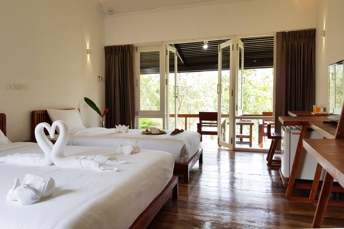 Quarto de hotel com duas camas, área de refeições e vista para o verde.
