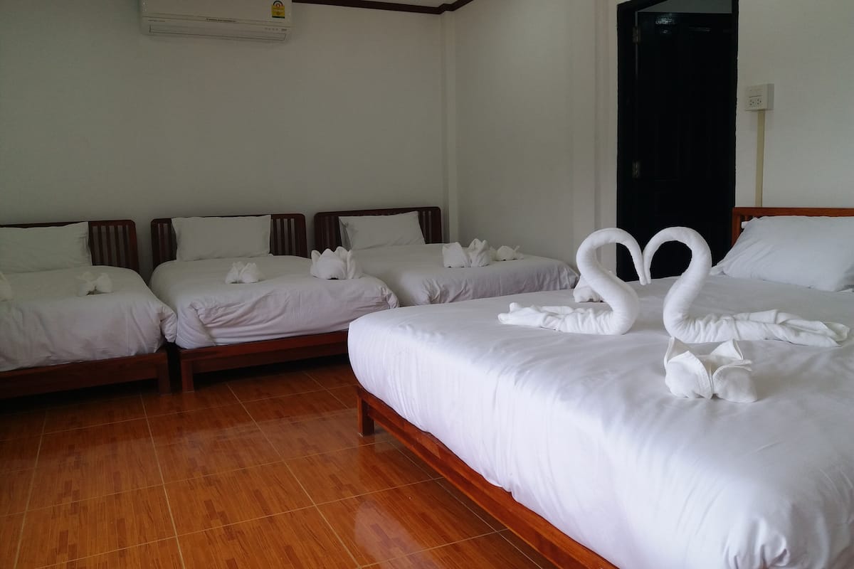 Quarto de hotel com três camas, cada uma com roupas de cama e toalhas brancas dispostas em formato de cisne.