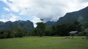 Um campo gramado com um pequeno edifício e uma montanha ao fundo.