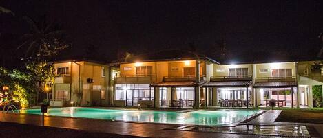 Um hotel de vários andares com piscina, área de estar ao ar livre e fachada bem iluminada.