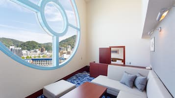 Quarto de hotel moderno com uma janela grande que oferece vista para a cidade, um sofá, uma pequena mesa e um armário.