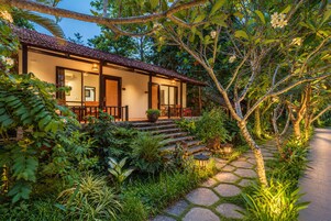 Uma casa com telhado em telhas, varanda com assentos e um caminho de pedra que leva à entrada.