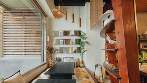 Um interior moderno com área de refeições, persianas de madeira, mesa preta e uma estante com objetos decorativos.