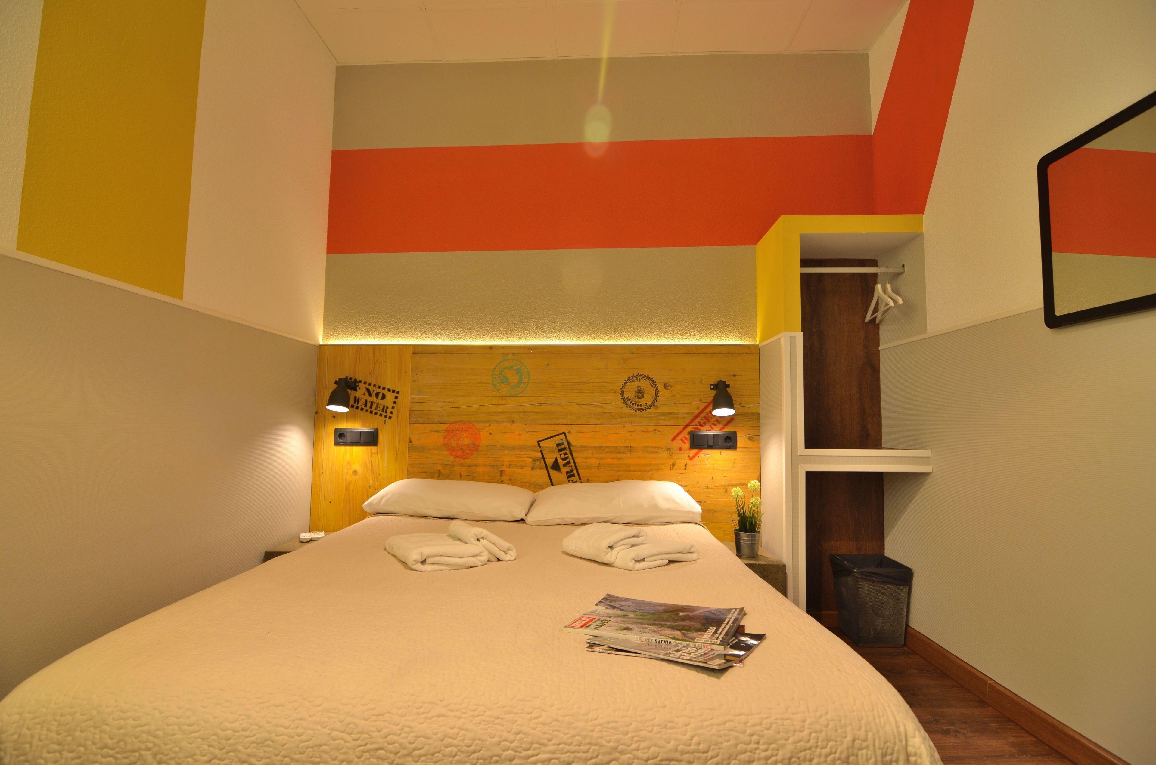 Quarto de hotel com cama, mesa de cabeceira, abajur, relógio de parede e espelho.