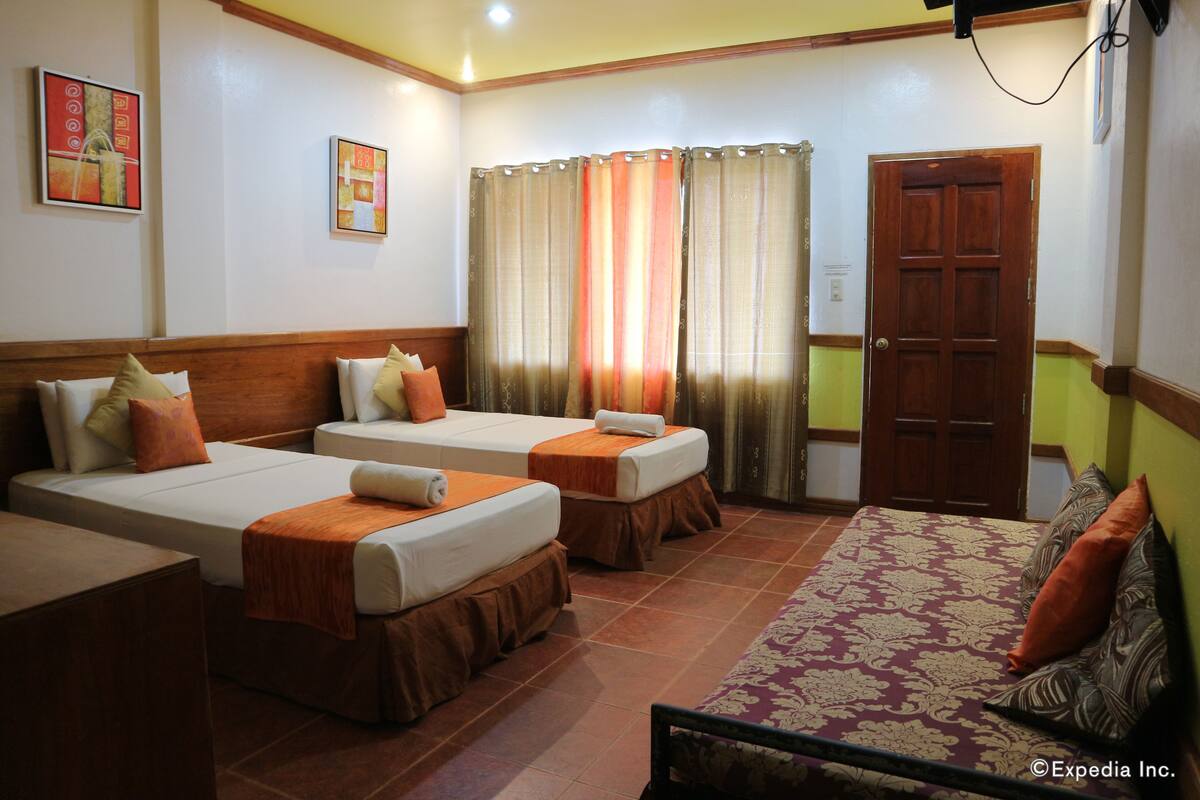 Quarto de hotel com três camas de solteiro, uma cama-sofá e uma porta de madeira.