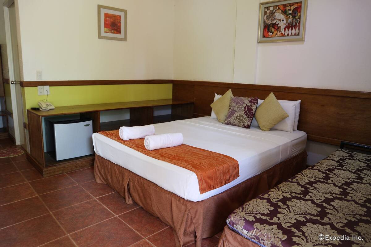 Quarto de hotel com uma cama, uma mesa com telefone e um pequeno frigorífico.