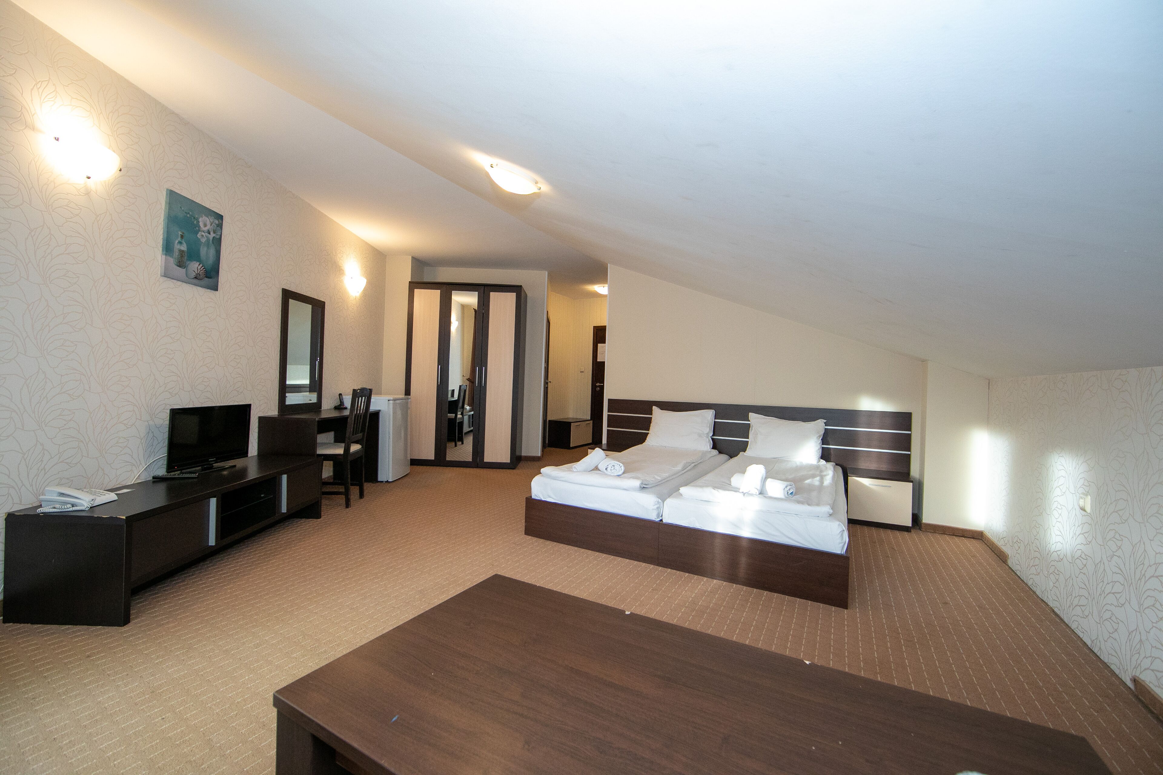 Quarto de hotel com cama, televisão, escrivaninha e espelho.