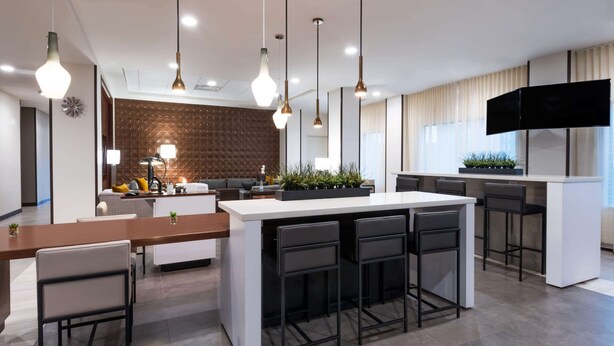 Cozinha moderna com ilha central, banquetas, iluminação pendente e televisão de tela plana.