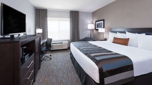 Quarto de hotel com uma cama grande, televisão de tela plana, escrivaninha com cadeira, abajur e janela com cortinas.