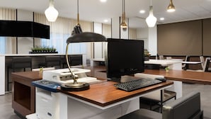 Um escritório moderno com uma mesa de madeira, um computador de mesa, uma impressora e um monitor de tela plana grande. Há várias cadeiras e uma janela grande com cortinas.