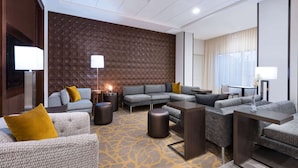 Um saguão de hotel moderno com parede estampada, várias áreas de estar e uma grande janela com cortinas.