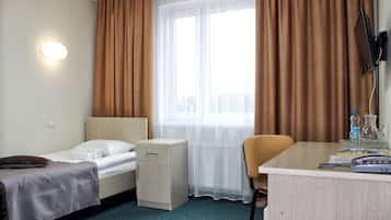 Quarto de hotel com duas camas de solteiro, uma escrivaninha com cadeira, televisão presa na parede e uma janela grande com cortinas.