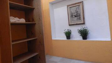 Um corredor com uma estante de madeira, um quadro na parede e duas plantas em vasos.