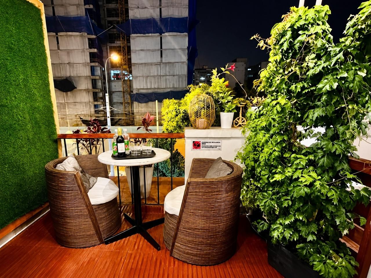 Terraço no telhado com mobiliário de vime, uma mesa redonda e plantas em vasos.
