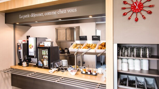 Espaço de buffet de café da manhã com máquina de café, pastelaria e diversos recipientes de comida.