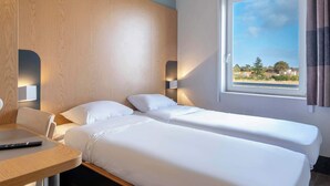 Quarto de hotel com duas camas de solteiro, uma escrivaninha e uma janela com vista para a paisagem.