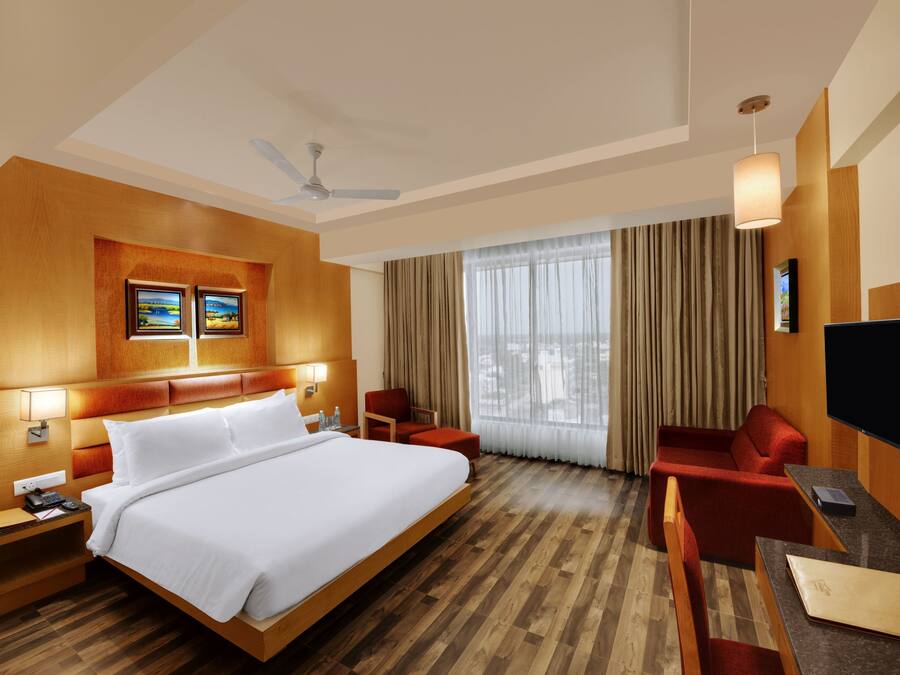 Quarto de hotel com uma cama grande, uma escrivaninha com cadeira, televisão e janela com cortinas.