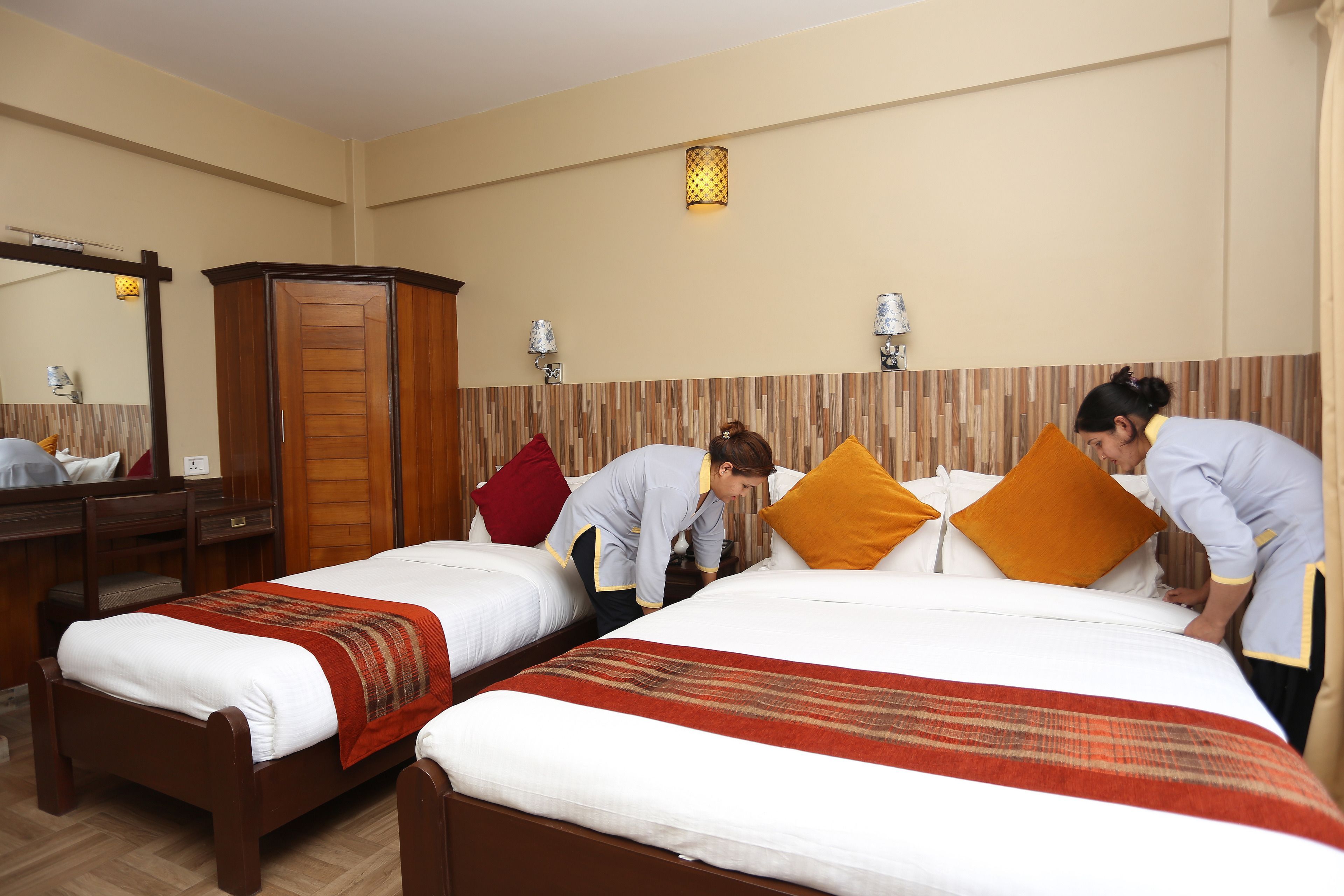 Quarto de hotel com duas camas, cabeceiras de madeira, um guarda-roupa e um espelho.