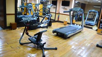 Uma academia com diversos equipamentos de exercícios, incluindo esteiras e elípticos, sobre piso de madeira.