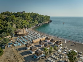 Um resort à beira-mar com cabanas de palha, espreguiçadeiras e área de piscina.