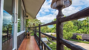 Um deck de madeira com guarda-corpo, uma luminária pendente e vista para vegetação exuberante.