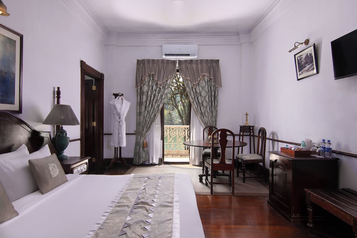 Quarto de hotel com cama, escrivaninha, cadeira, televisão e janela com cortinas.