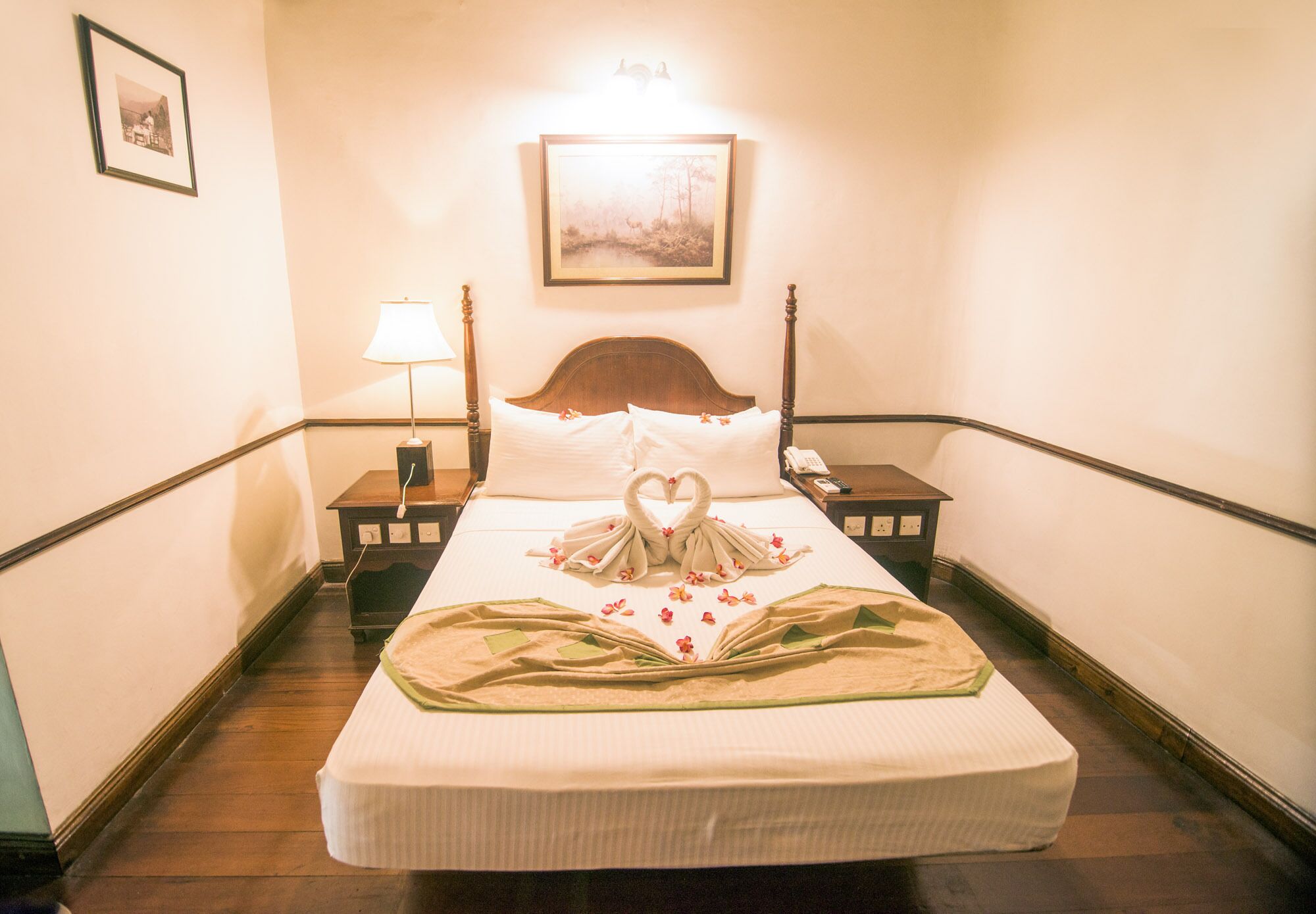 Uma cama bem arrumada com arranjo de toalhas em formato de coração, um abajur e um quadro na parede.