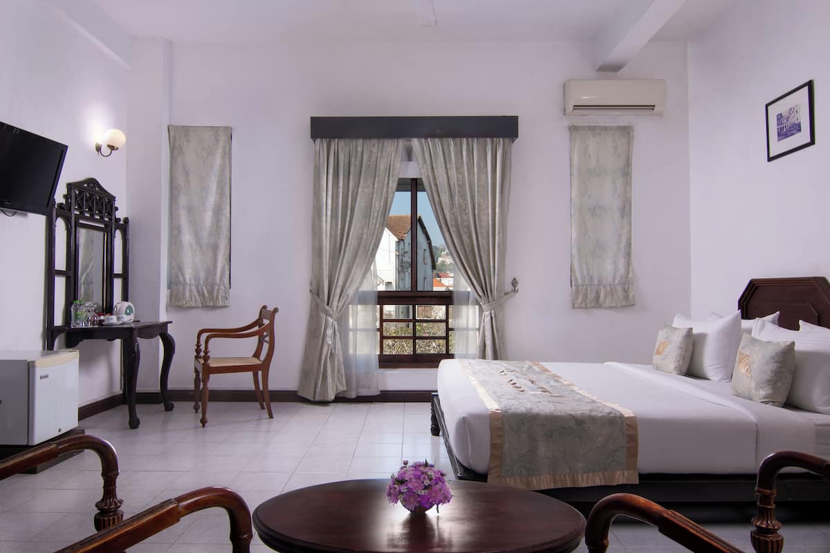 Quarto de hotel com cama, escrivaninha com computador, cadeira e janela com cortinas.