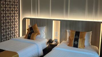 Quarto de hotel com duas camas, um painel decorativo na parede e uma mesa de cabeceira com telefone e abajur.
