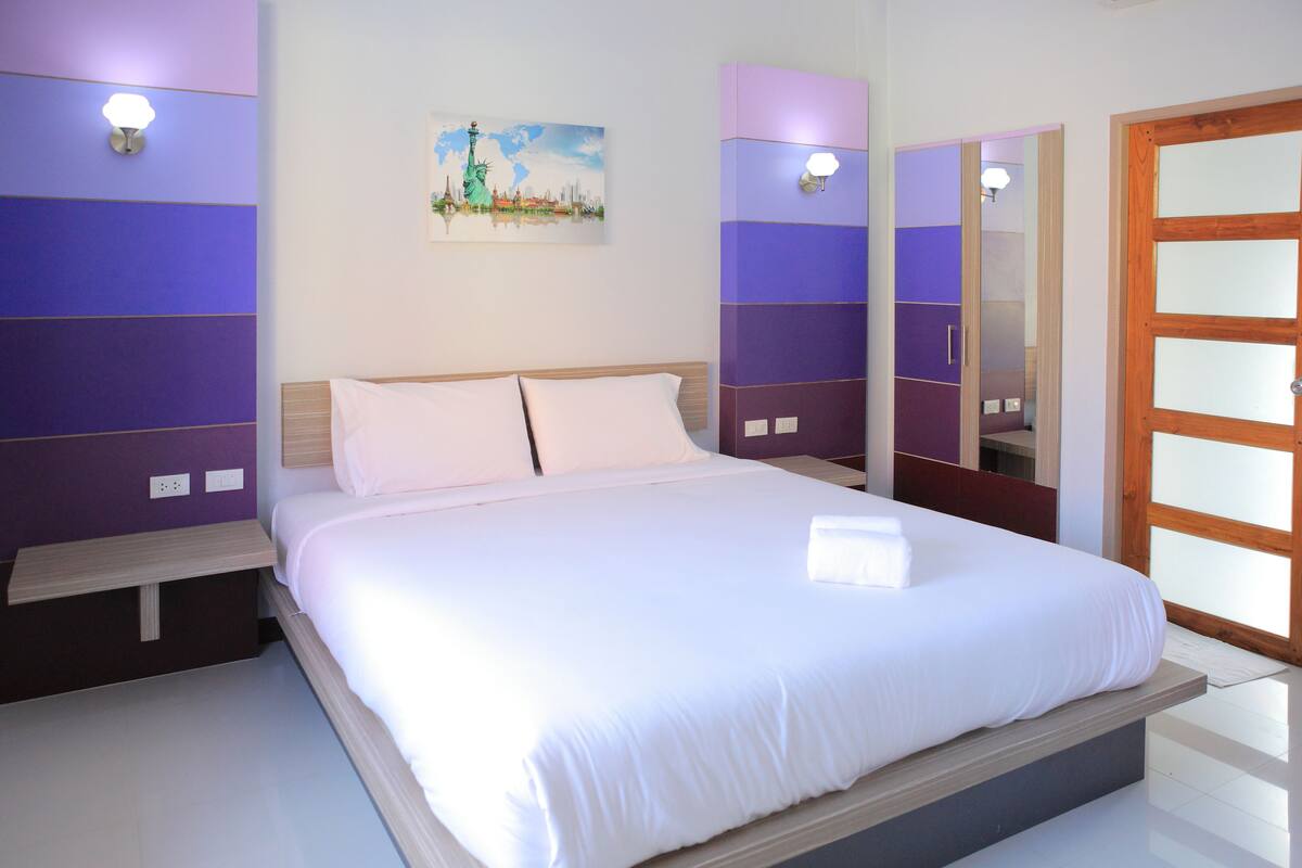 Cama bem arrumada em quarto de hotel, com um espelho grande e uma pintura da Estátua da Liberdade na parede.