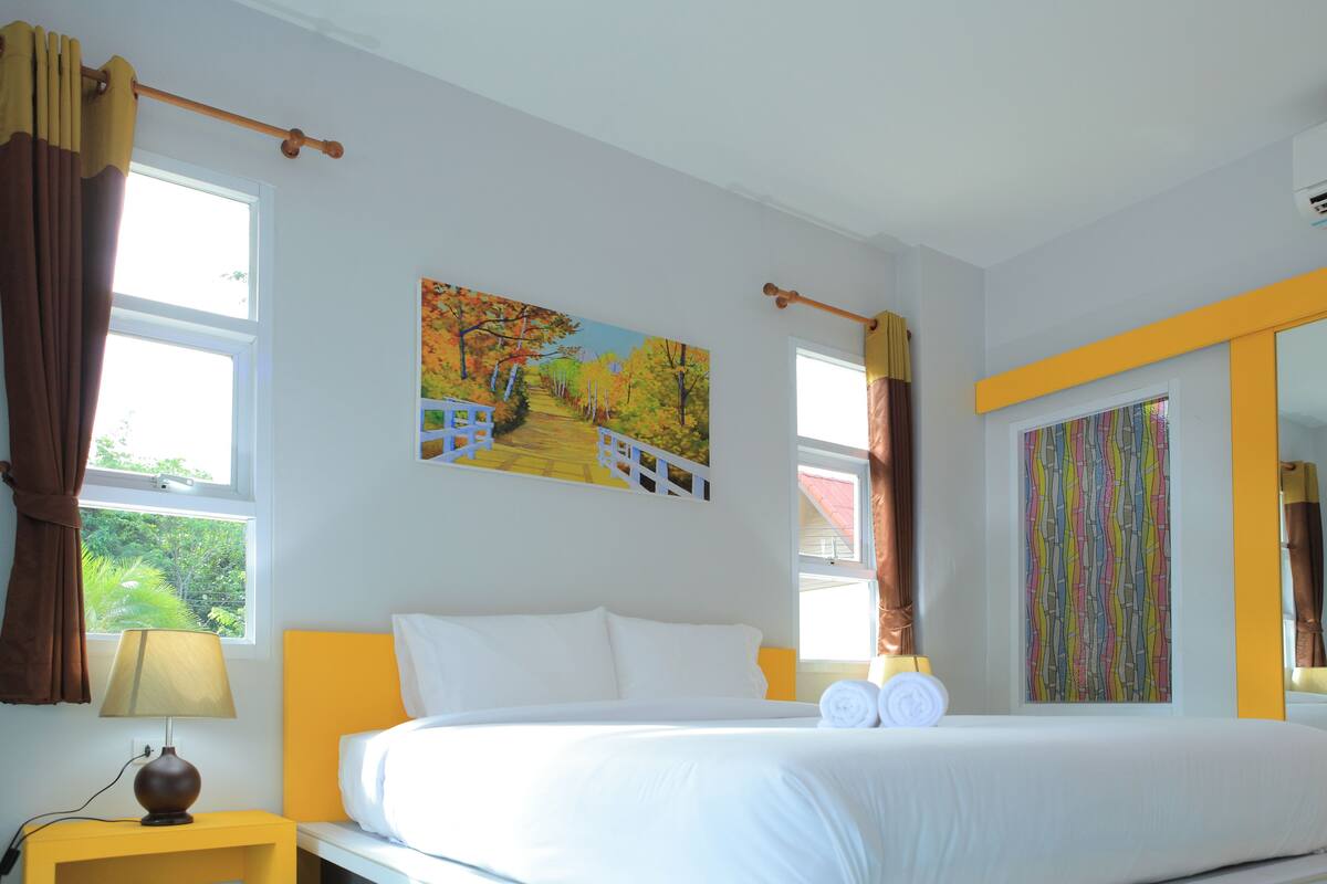 Quarto com cama, mesa de cabeceira, um quadro e janela com cortinas.