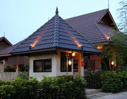 Uma casa com telhado inclinado, um pequeno alpendre com um candeeiro e uma cerca de madeira ao fundo.