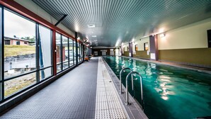 Piscina interna com vista desobstruída para o exterior através de amplas janelas, piso revestido e escada de metal.
