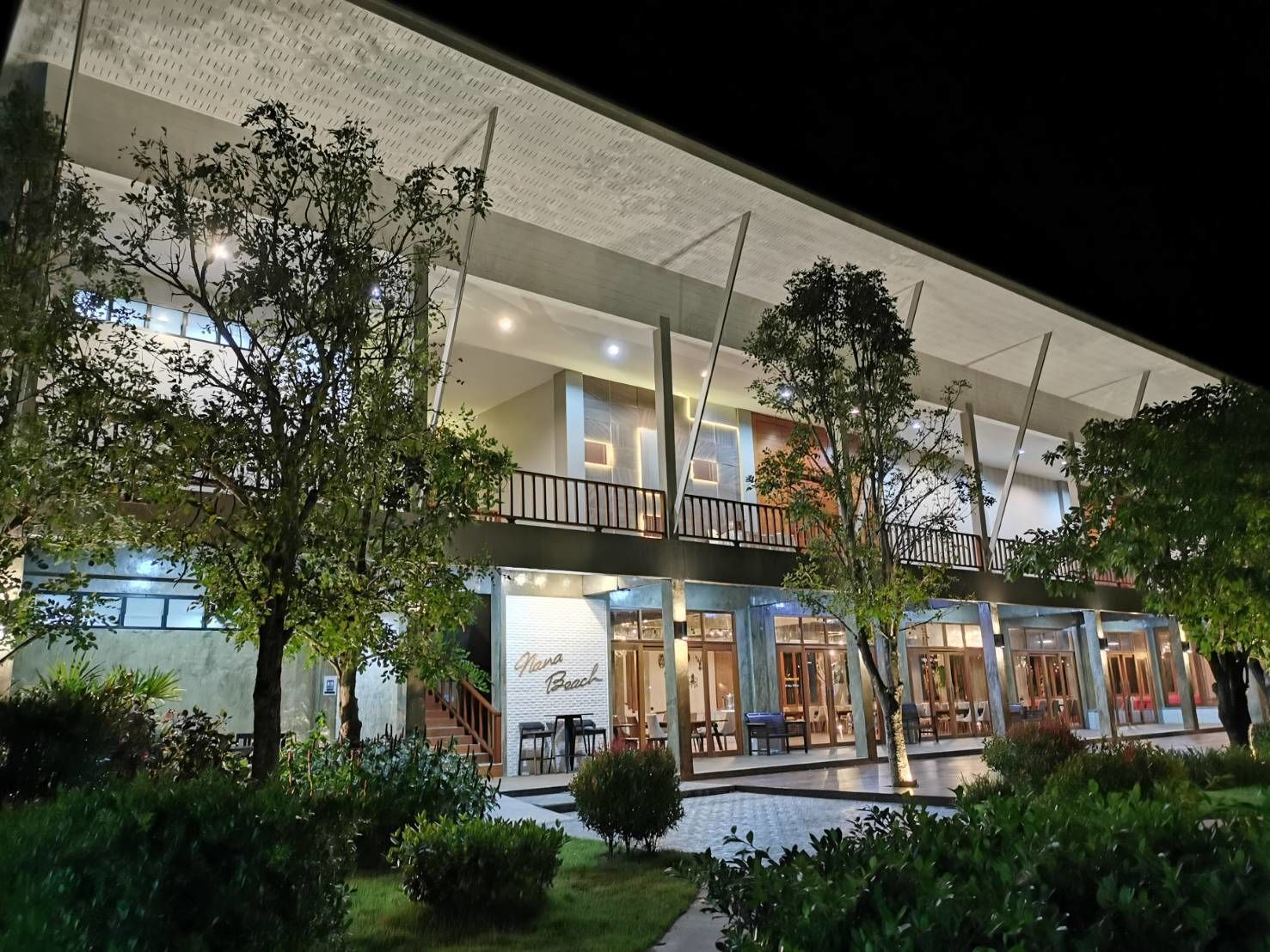Um hotel com estrutura em dois andares, área de estar externa e um jardim bem cuidado.