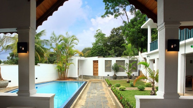 Uma área de piscina com um caminho de pedra que leva a um edifício branco com colunas e um corredor coberto.