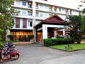 Hotel com design moderno, apresentando uma entrada convidativa com uma placa, área de estacionamento coberta e um jardim bem cuidado.