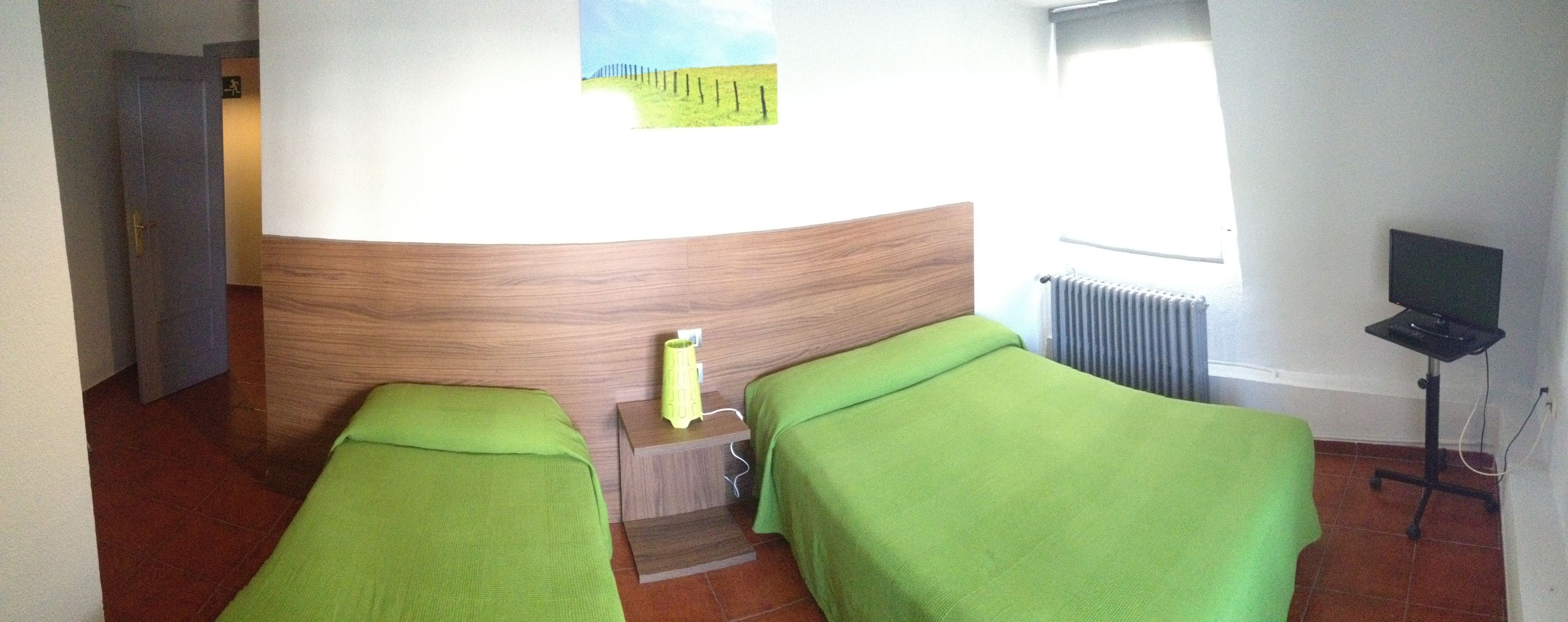 Quarto com duas camas, um radiador, uma TV sobre um suporte e um quadro na parede.