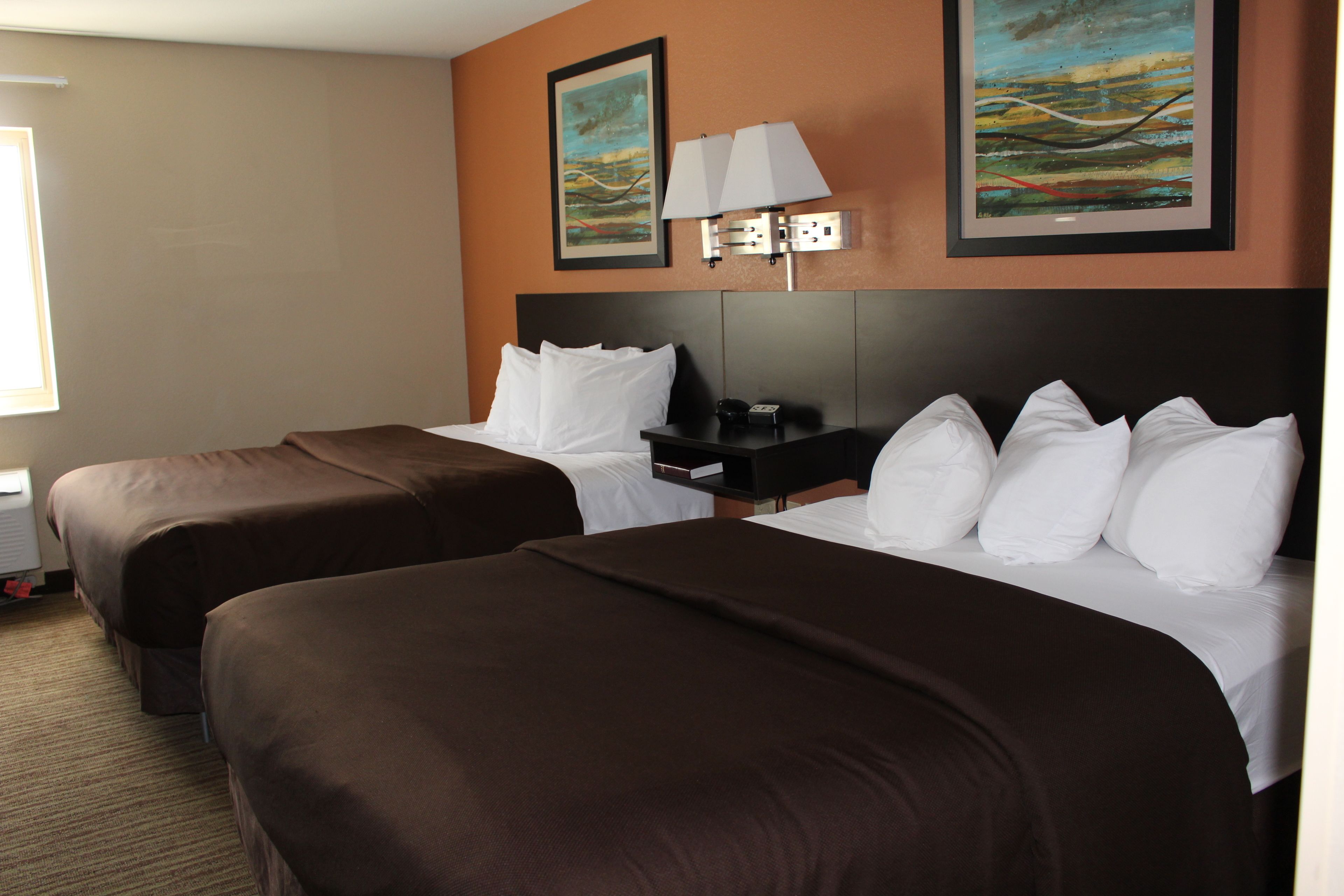 Quarto de hotel com duas camas, uma mesa de cabeceira e duas pinturas na parede.