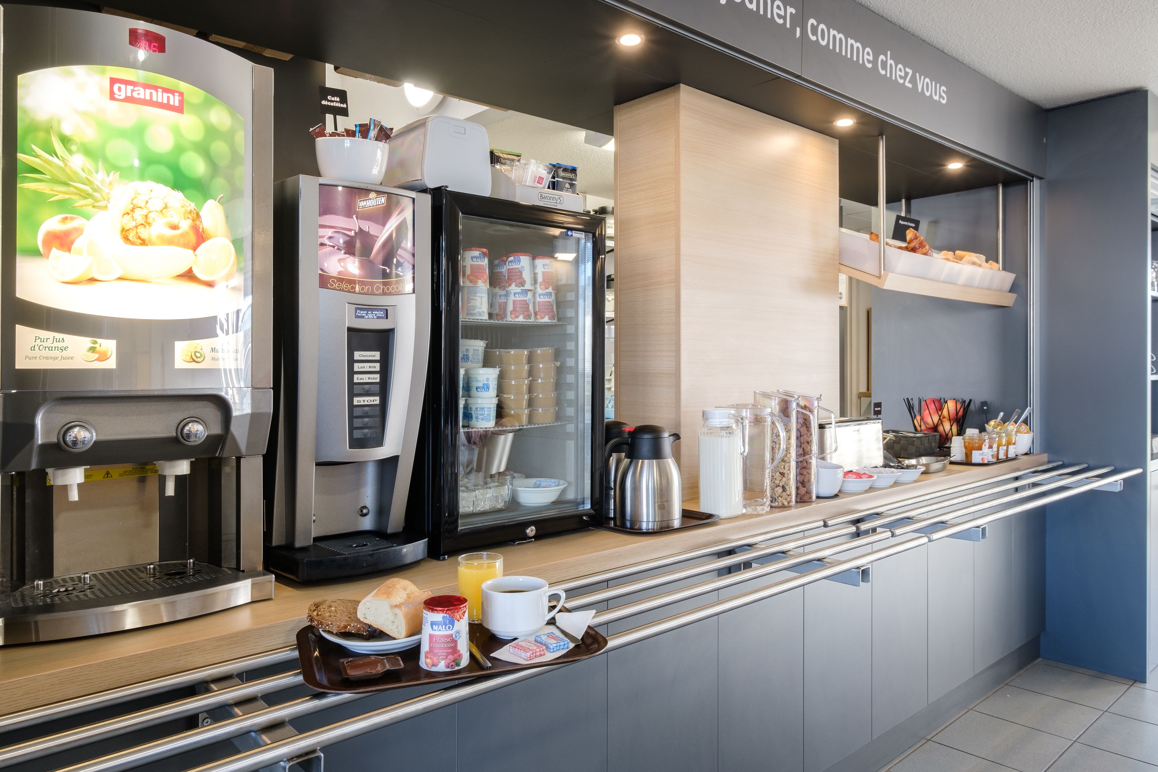 Uma área de refeições moderna com máquina de café, frigorífico e seleção de produtos para o pequeno-almoço.