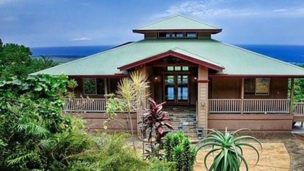 Um edifício de dois andares com telhado verde, rodeado por vegetação exuberante e com vista para um corpo de água.