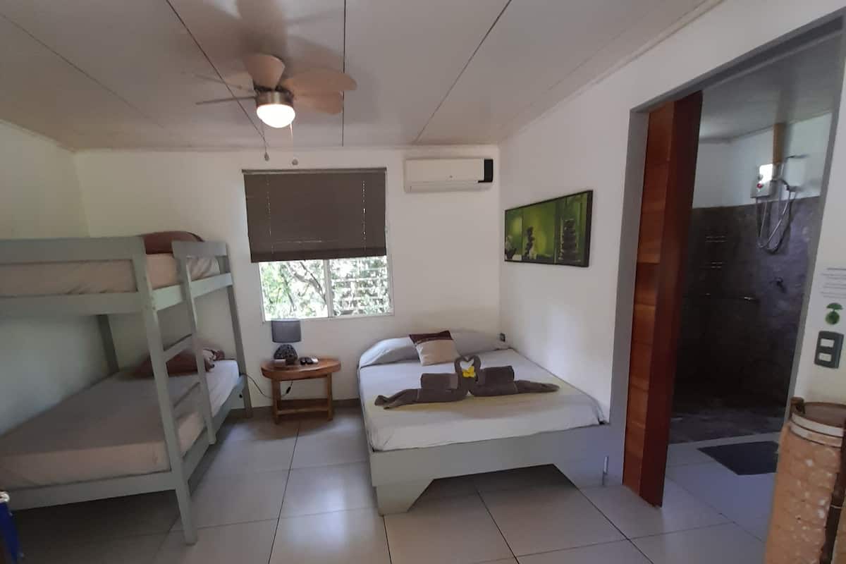 Um dormitório com beliches, um ventilador de teto, uma janela com persianas e uma área de chuveiro.