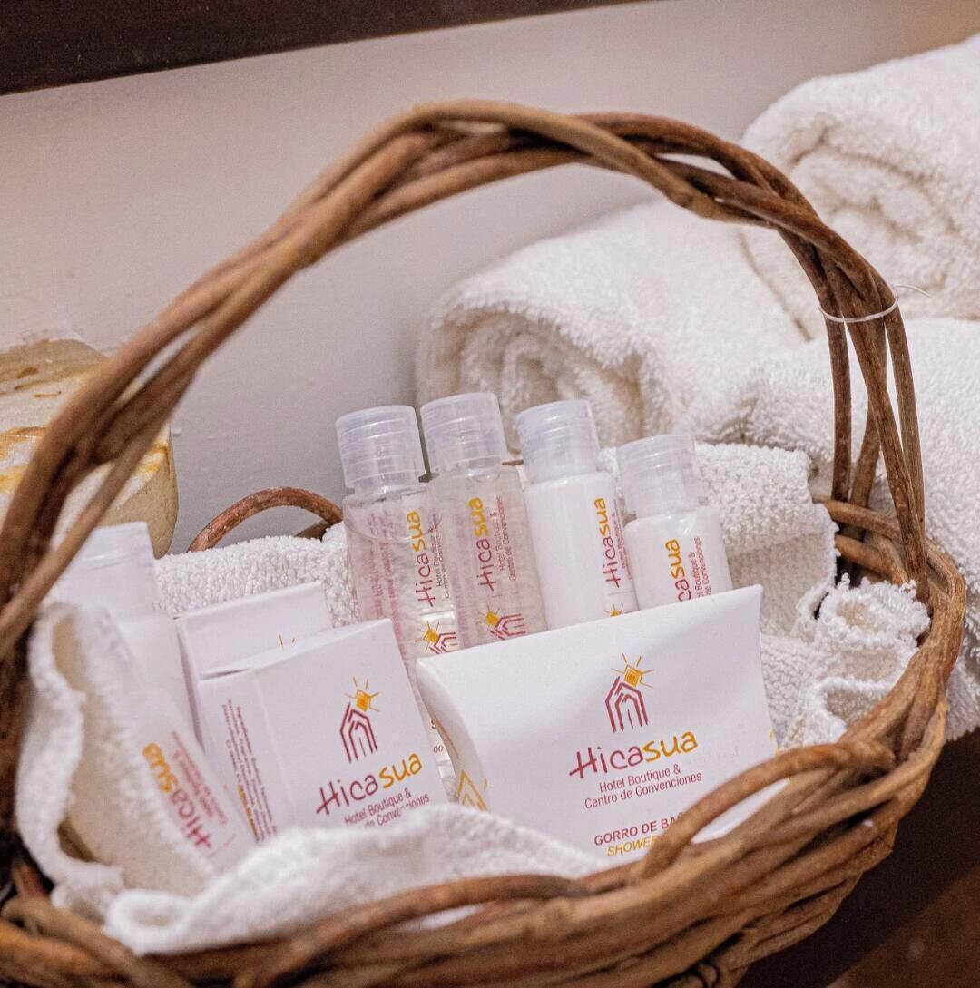 Uma cesta de vime com produtos de higiene e toalhas, com a marca 'Hicasua' visível nas embalagens.