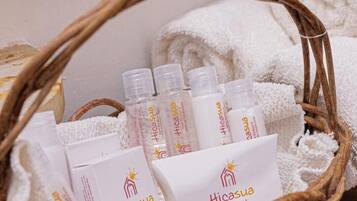 Uma cesta de vime com produtos de higiene e toalhas, com a marca 'Hicasua' visível nas embalagens.