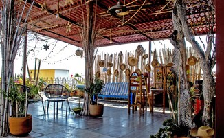 Uma área de varanda ao ar livre com estruturas de bambu, plantas em vasos e um banco listrado em azul.