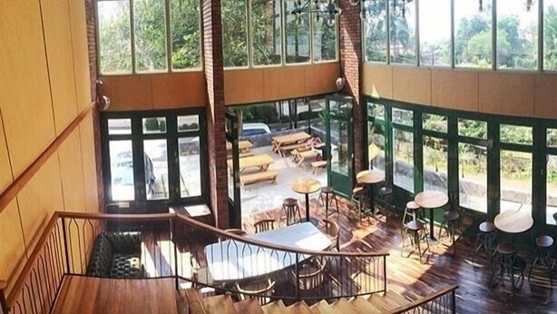 Restaurante com escada de madeira que dá acesso a uma área de refeições com mesas e cadeiras redondas.