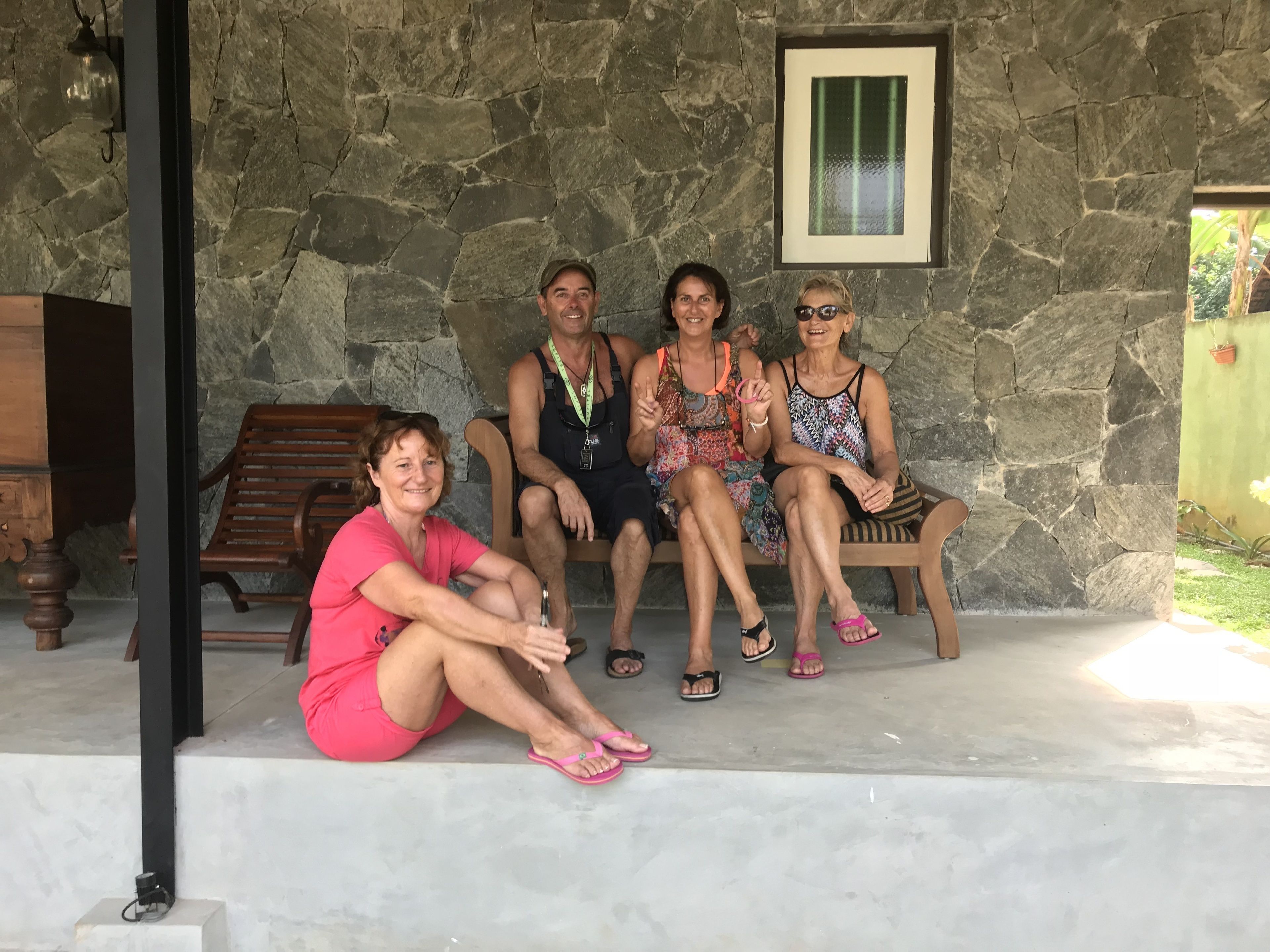 Quatro pessoas sentadas num banco numa área de paredes de pedra com uma moldura na parede.